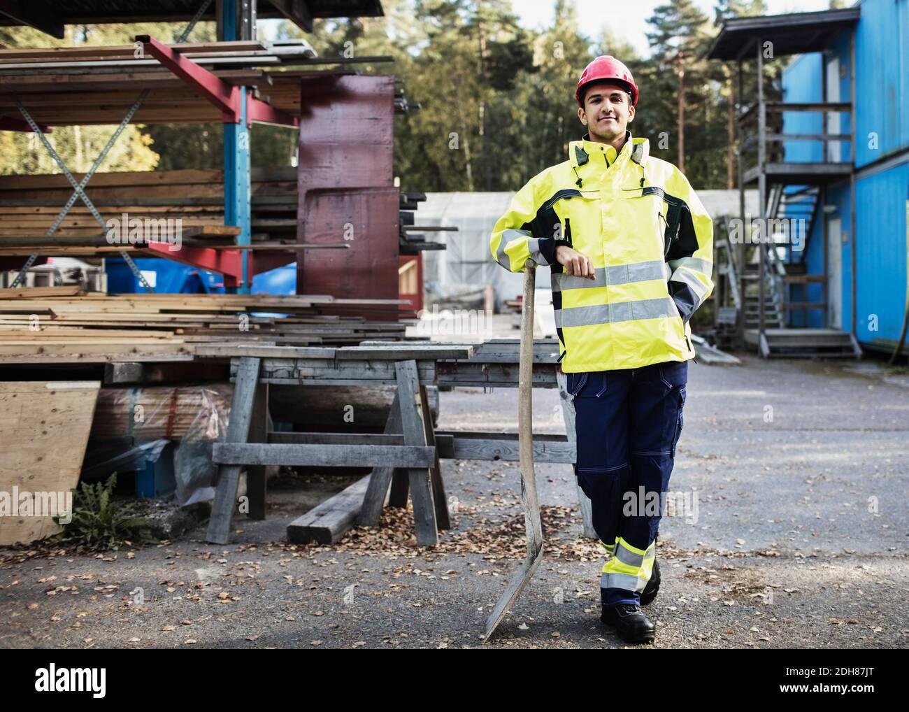 Full length portrait of carpentry student leaning on spade outside ...