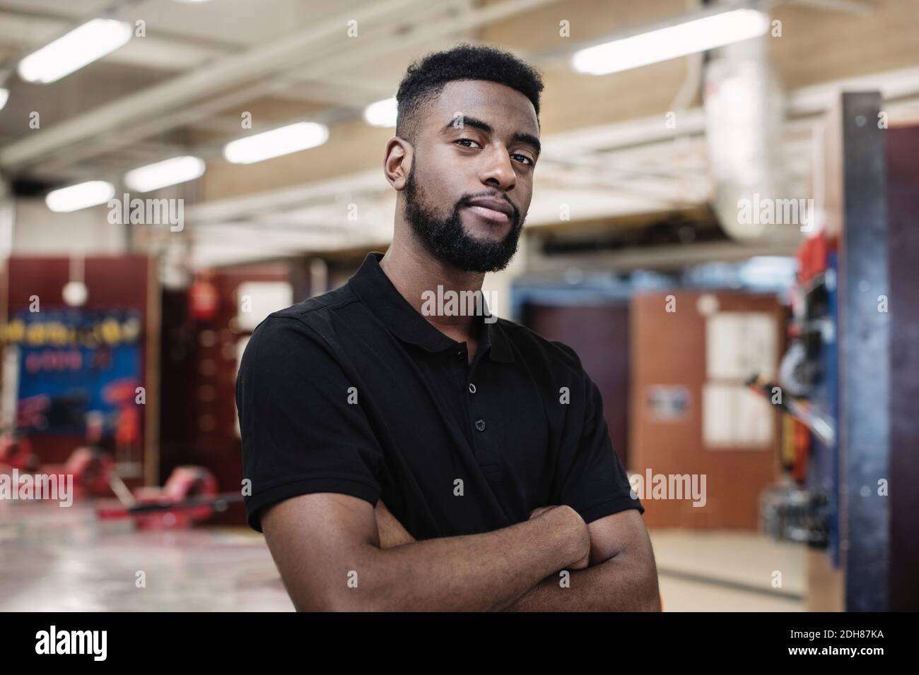 Portrait of male auto mechanic student standing arms crossed at ...