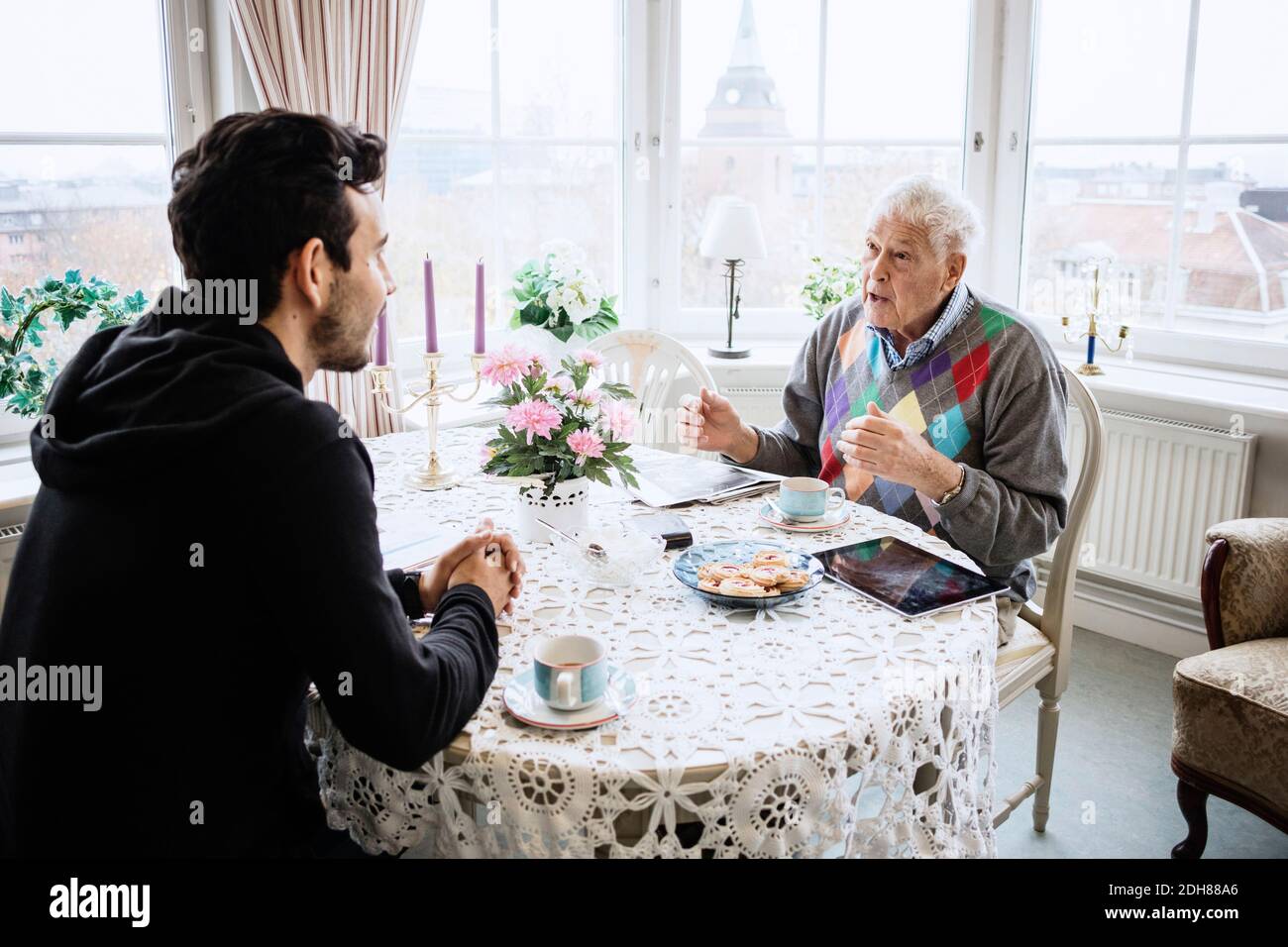 Senior man communicating to caretaker at dining table in nursing home ...