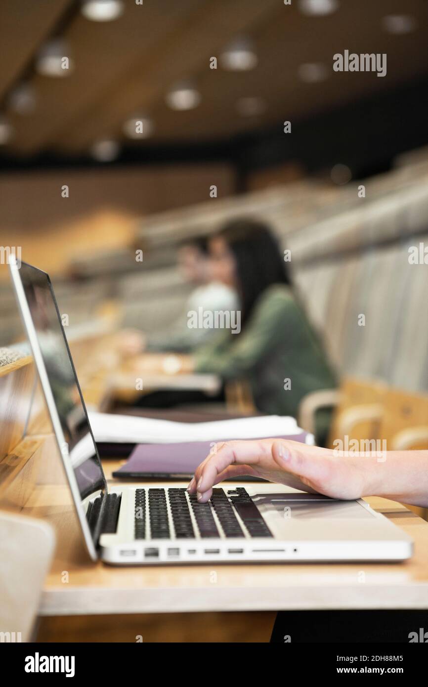 Close-up of human hand typing on laptop keyboard with people in ...