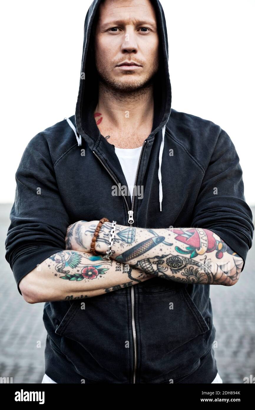 Portrait of a tattooed man in hooded jacket with arms crossed Stock Photo - Alamy