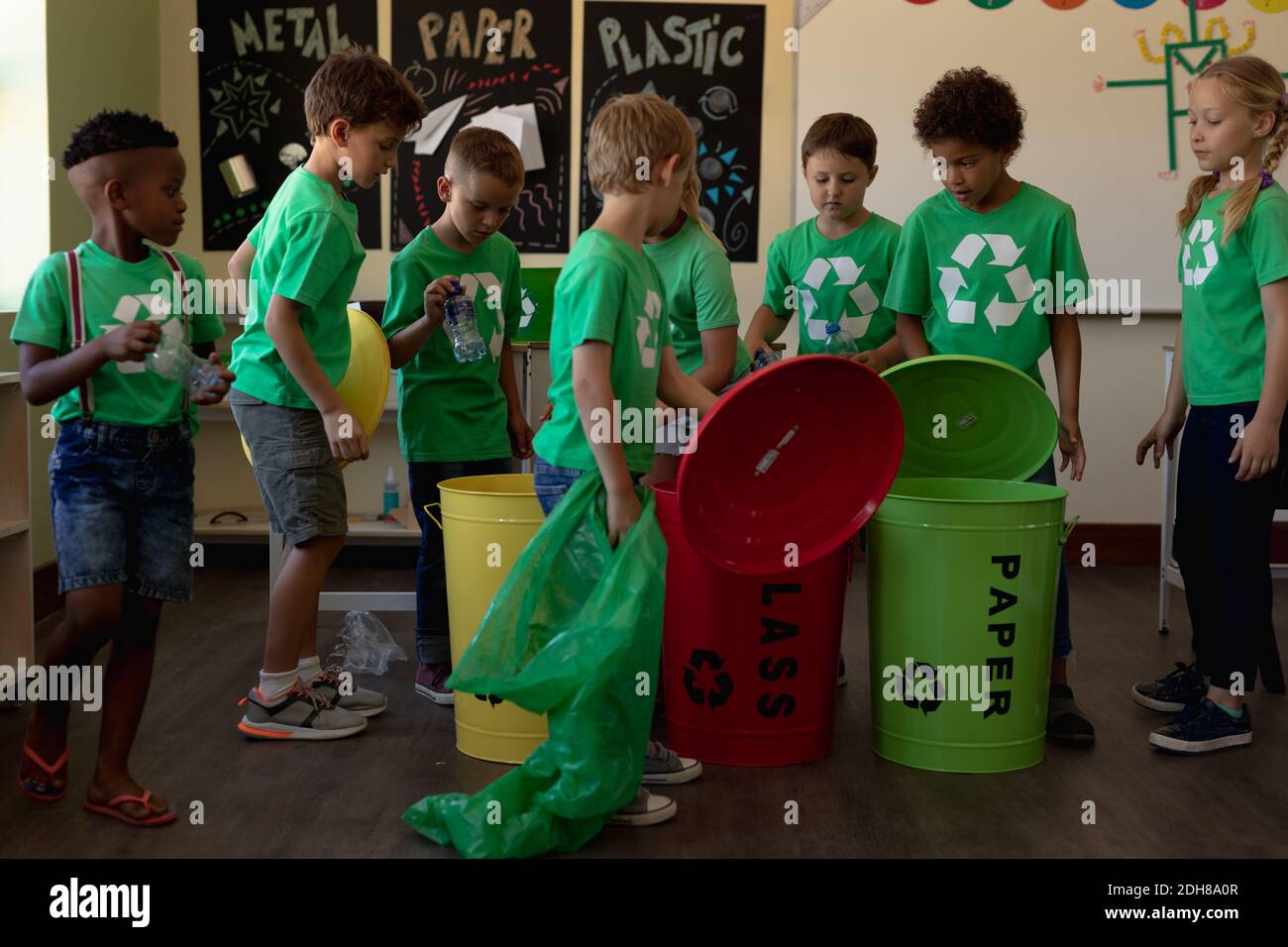 Group of schoolchildren holding color coded recycling bins and bags in ...