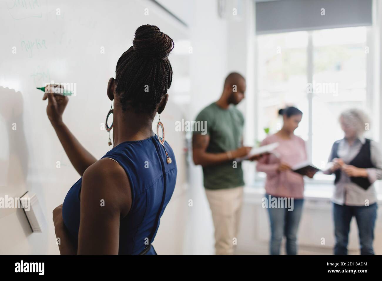 Woman holding pen looking at teacher and students standing in language ...