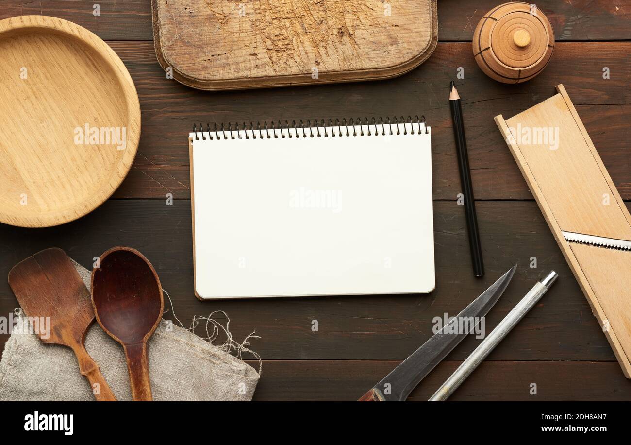 Open notebook with blank white sheets and kitchen utensils on brown ...