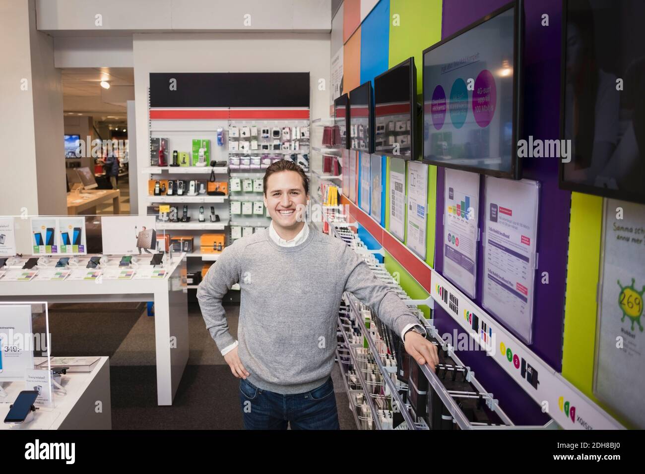 Portrait of cheerful salesman standing in electronics store Stock Photo ...