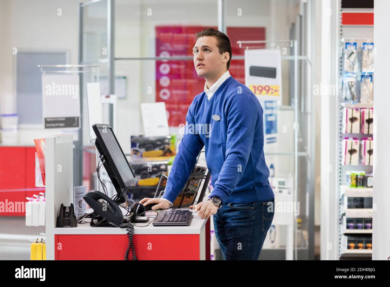 Salesman looking up while standing at counter in store Stock Photo - Alamy