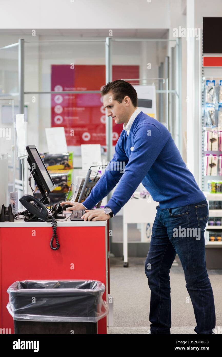Salesman using computer while leaning on counter in store Stock Photo ...