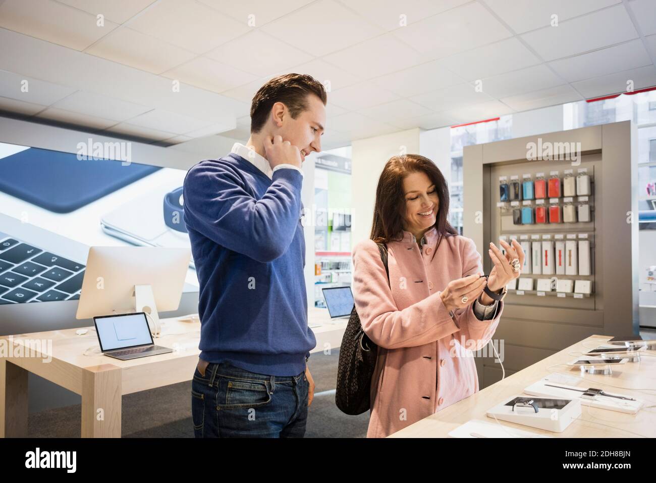 Happy female customer wearing smart watch while standing with salesman ...