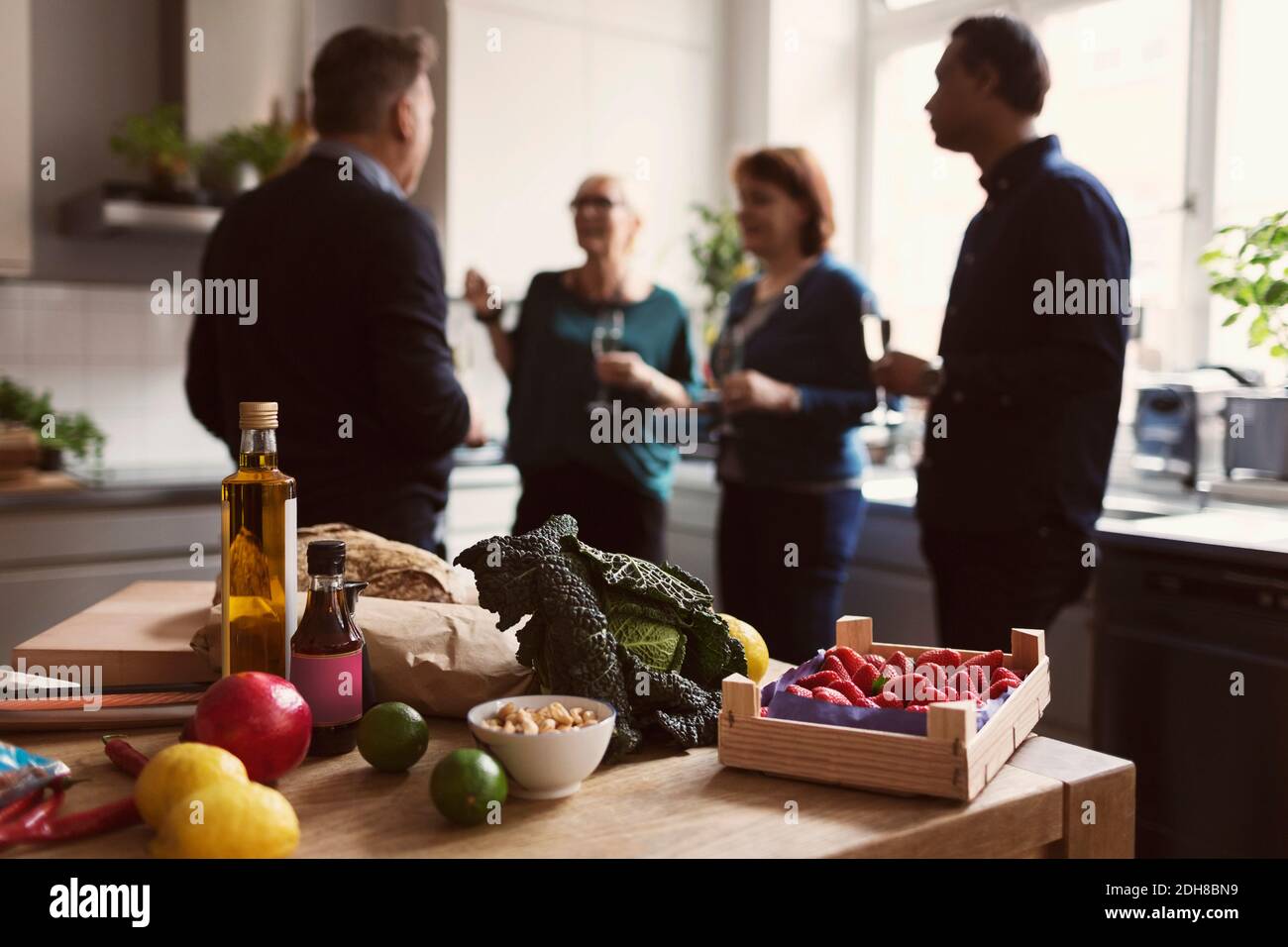 Food on table against friends talking in kitchen Stock Photo - Alamy