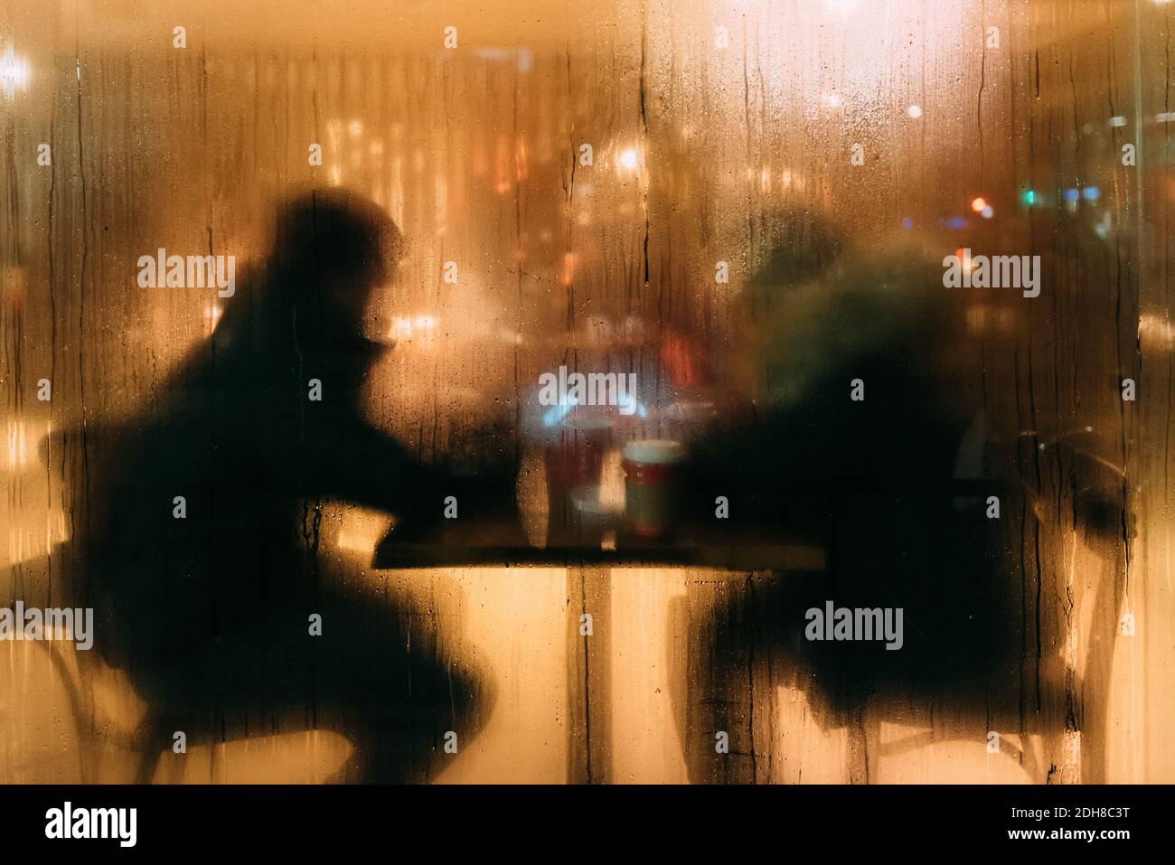 A closeup of a glass wall of a cafe covered in raindrops with two ...