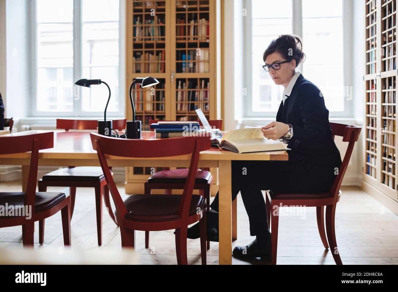 Side view of female professional reading book at table in law library ...