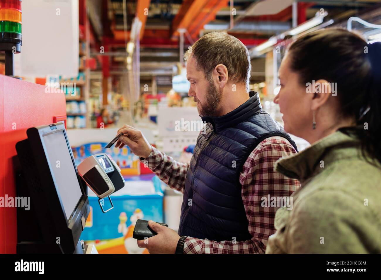 Man paying with credit card while standing with woman at supermarket ...
