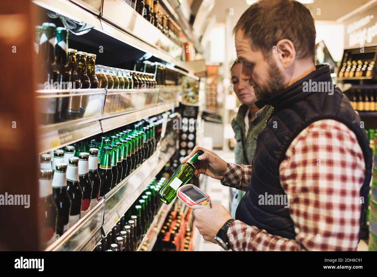Man using bar code reader on beer bottle while standing with woman in ...