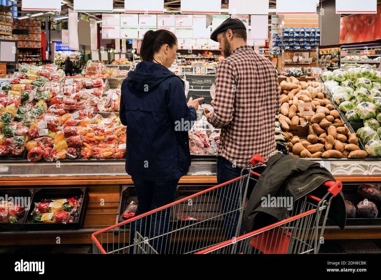 Rear view of couple choosing vegetables while standing at supermarket ...