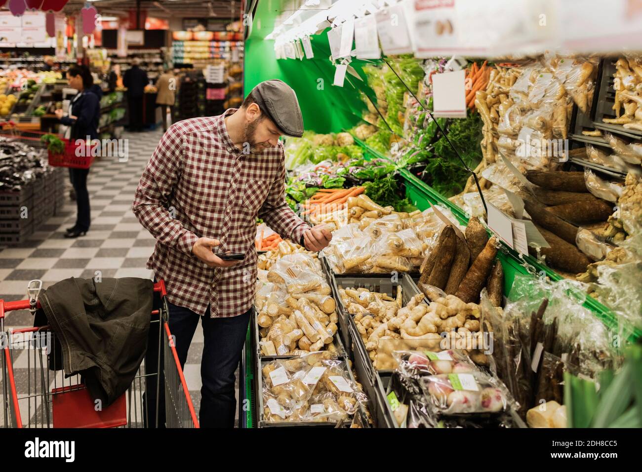 Man holding smart phone while buying root vegetable in supermarket ...