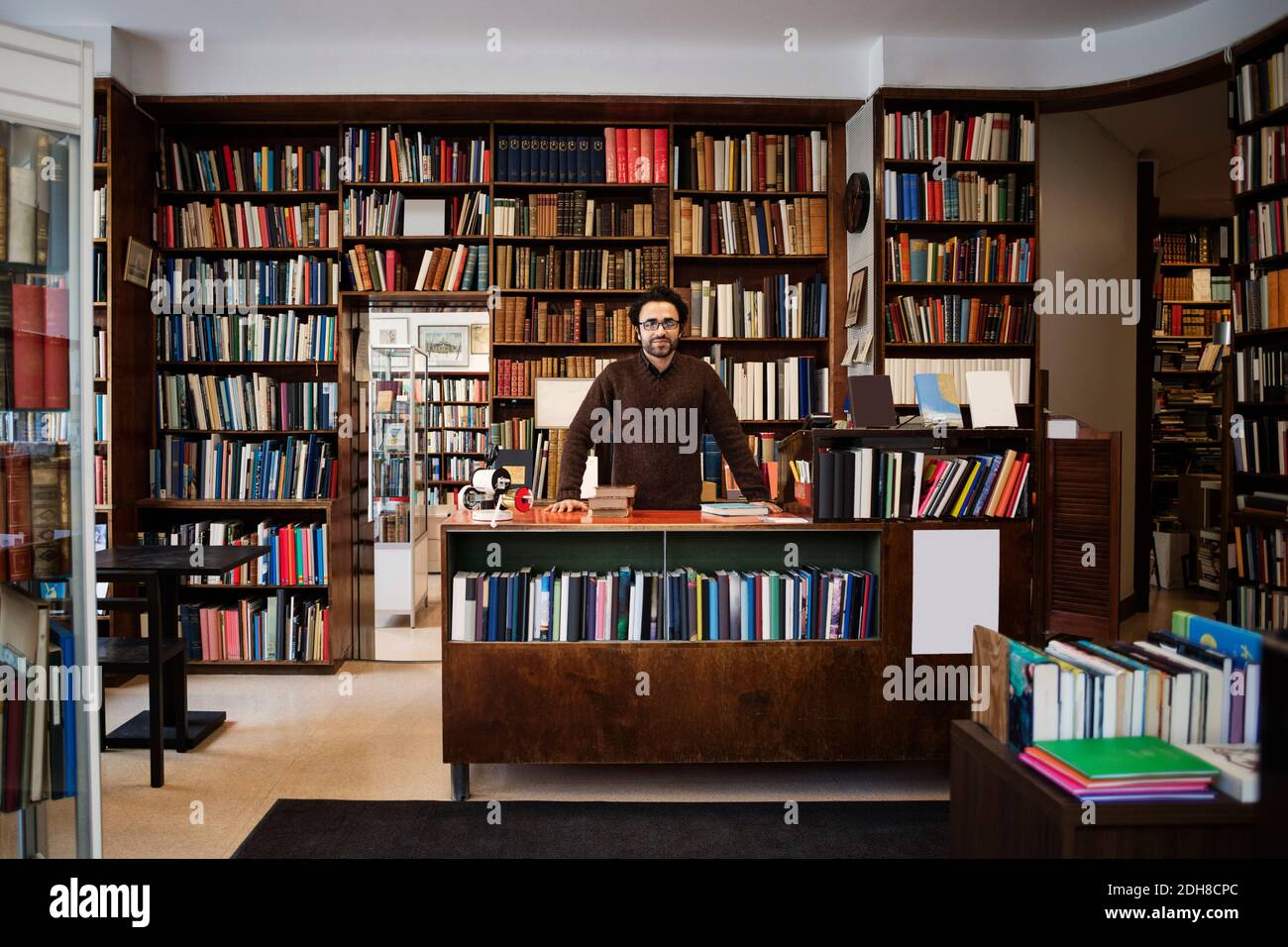 Portrait of owner standing against bookshelves in library Stock Photo ...