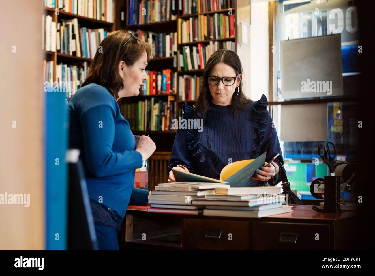 Female customer discussing with librarian standing in bookstore Stock ...