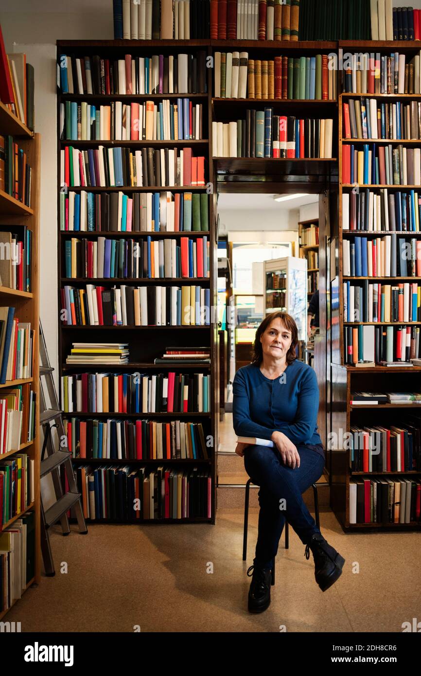 Portrait of confident owner sitting on chair in antique book shop Stock ...