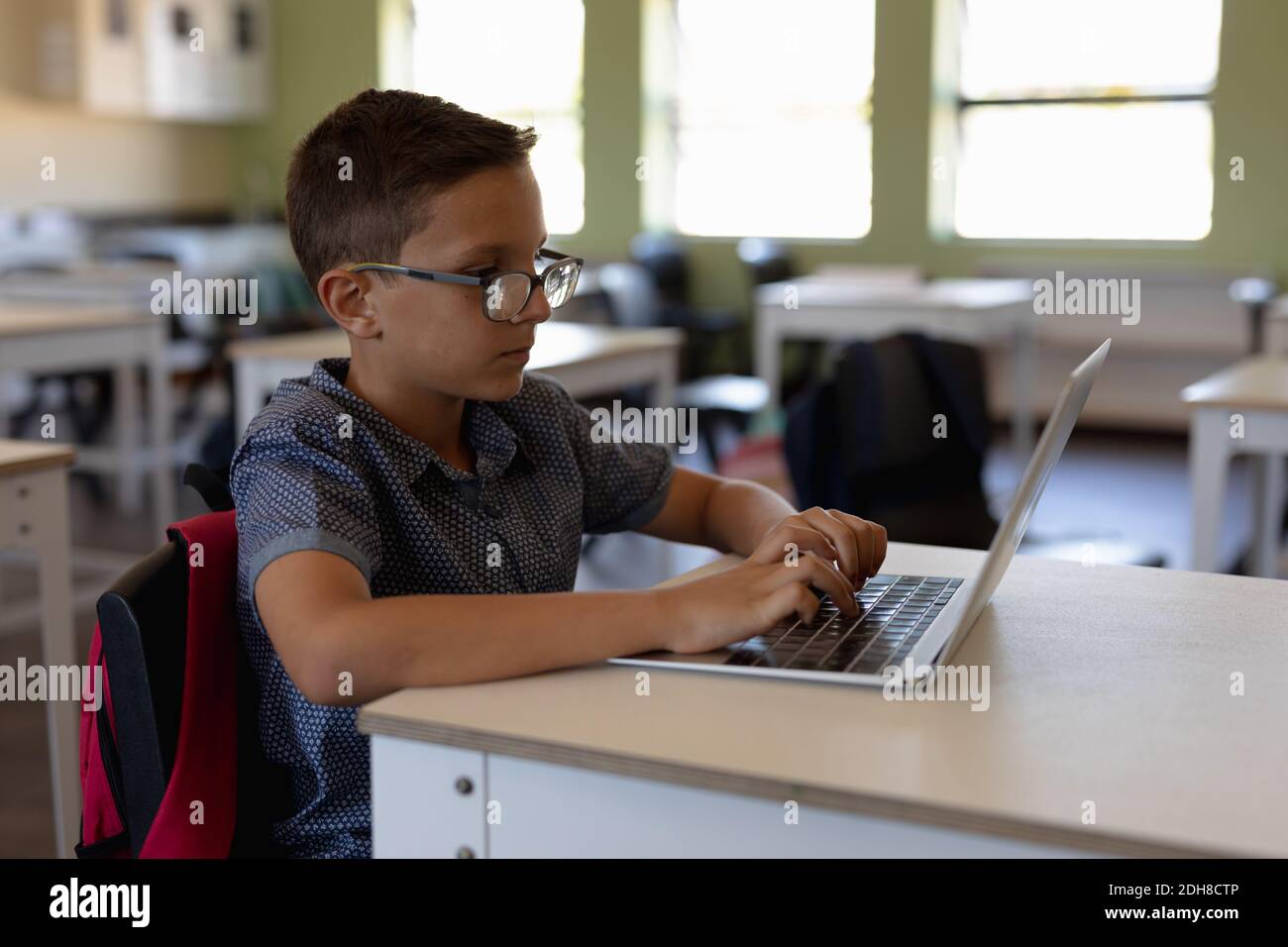 Schoolboy sitting at a desk using a laptop computer in an elementary school classroom Stock ...