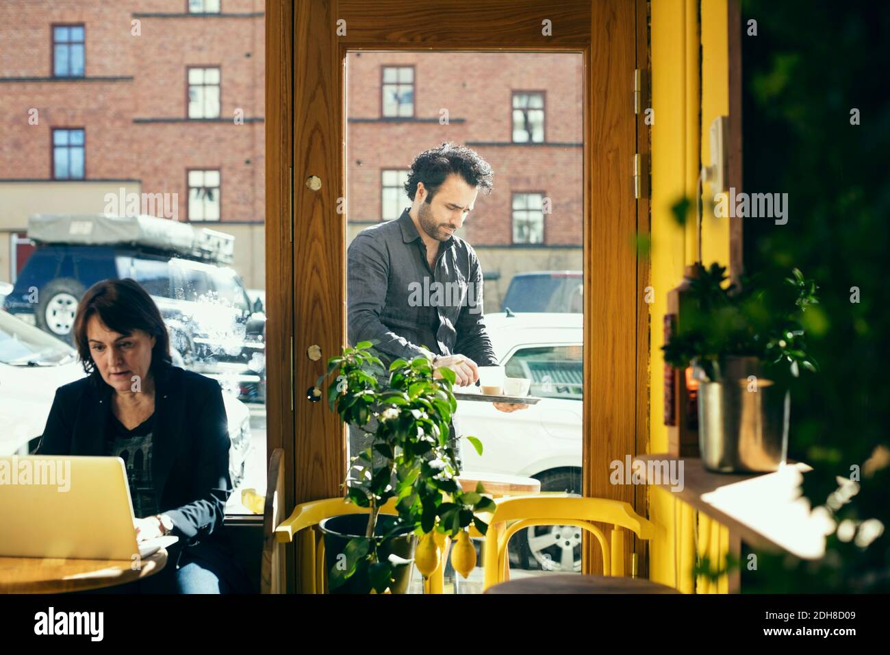Customer using laptop with waiter seen through glass door at cafe Stock ...