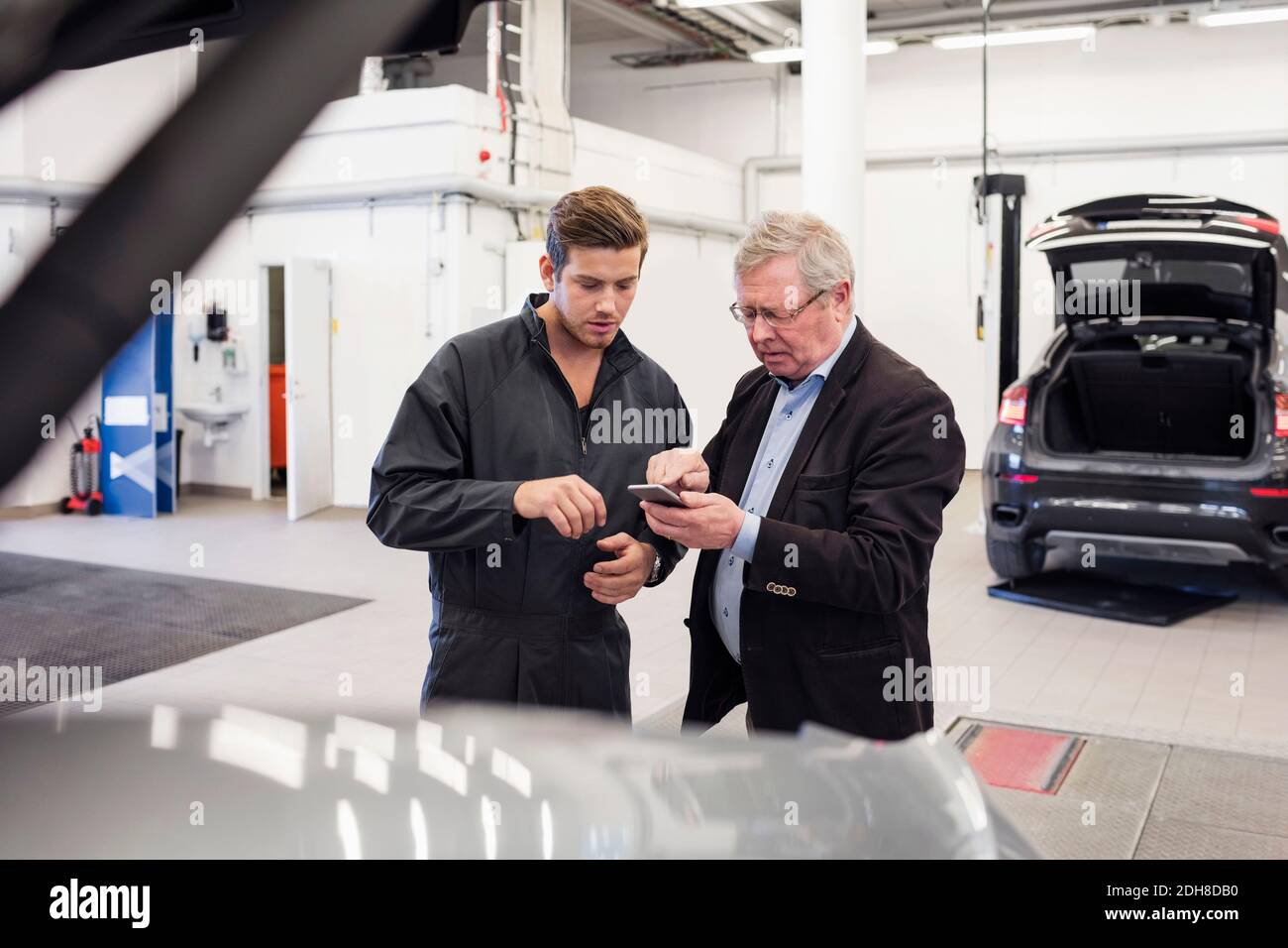 Male customer showing mobile phone to mechanic at auto repair shop ...