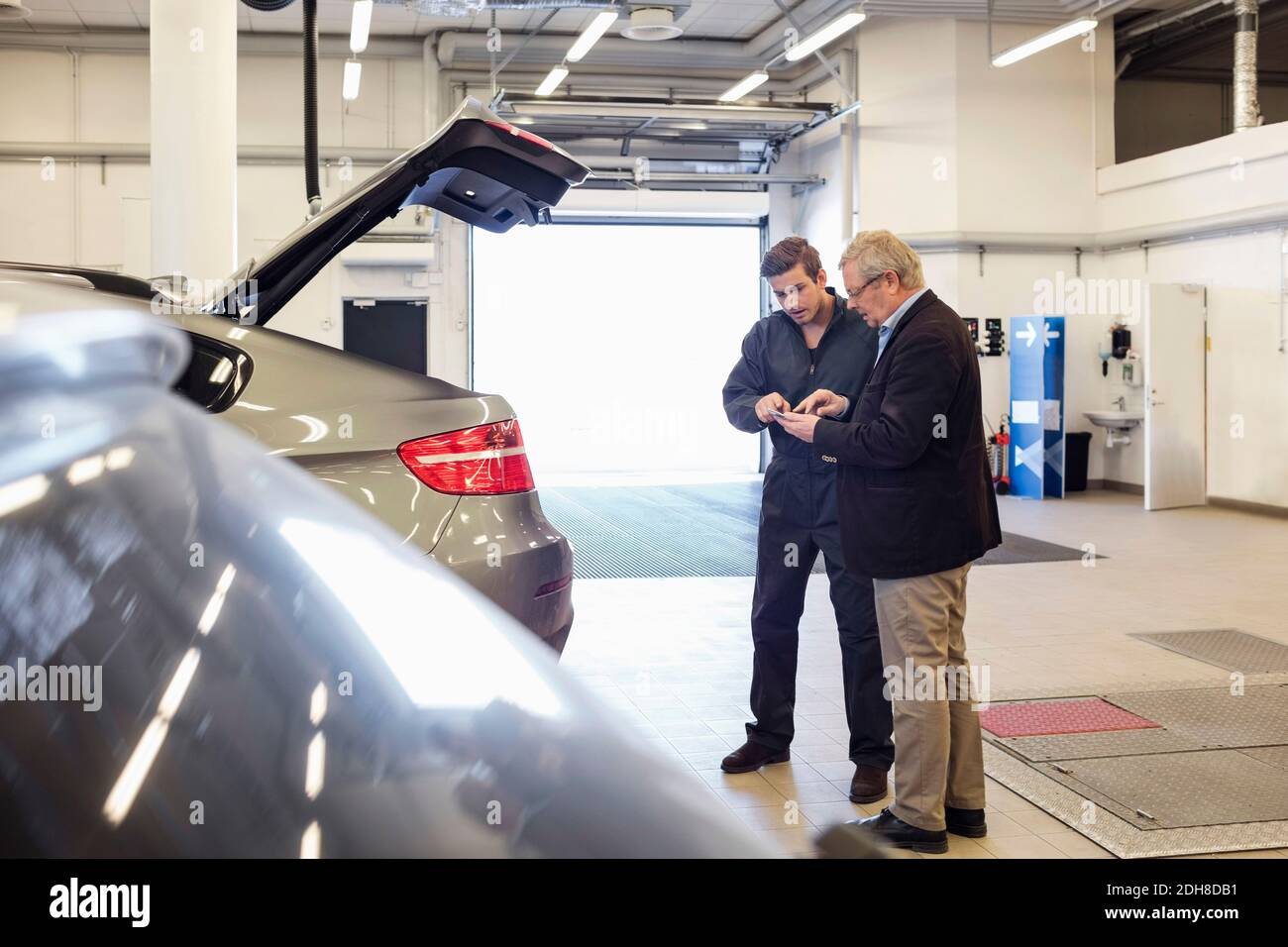 Customer and mechanic using mobile app while standing by car in repair ...