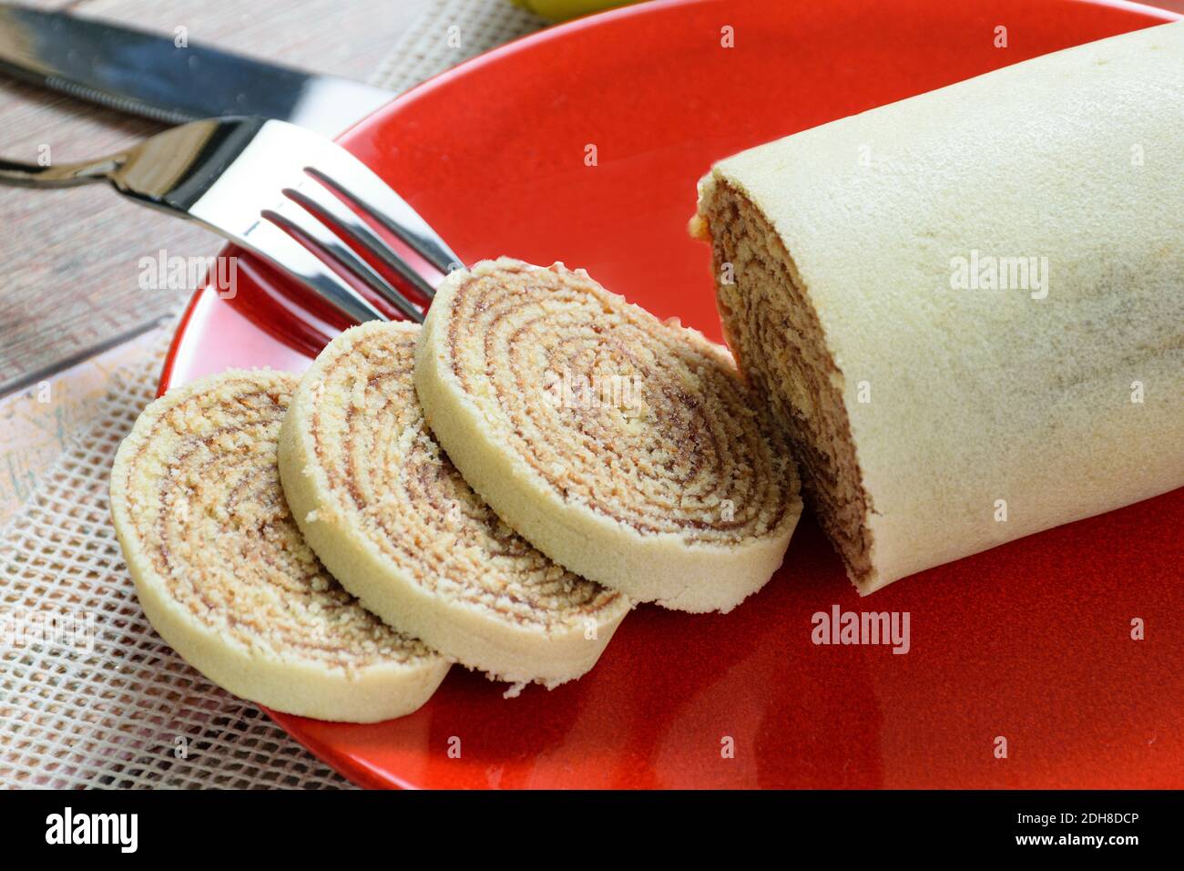 Closeup of sliced bolo de rolo (roll cake) on a red plate next to a ...