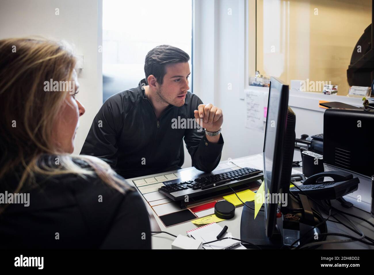 Owner explaining female client over computer in office at auto repair ...