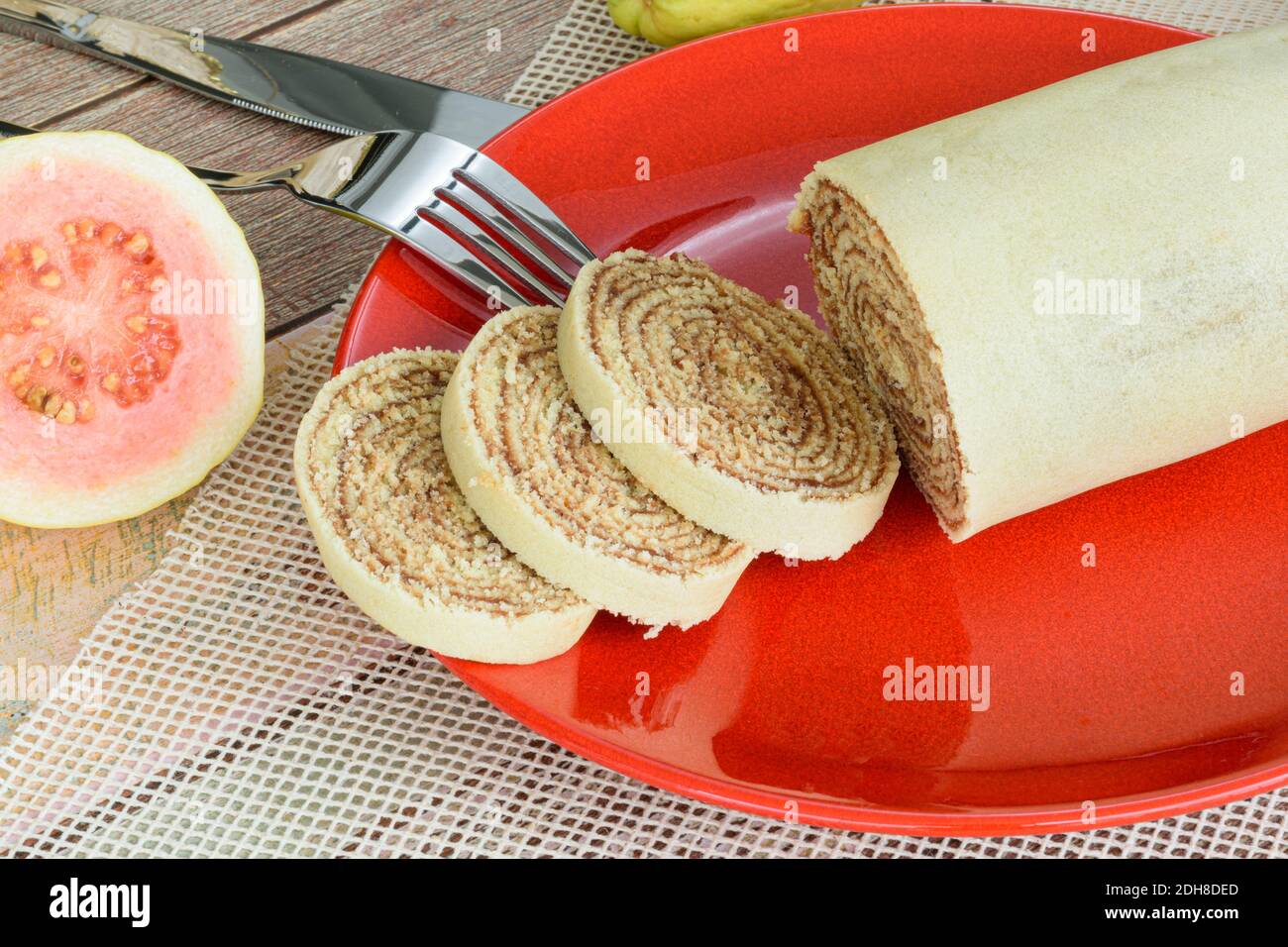 Bolo de rolo (roll cake) on a red plate next to a fork and sliced guava ...