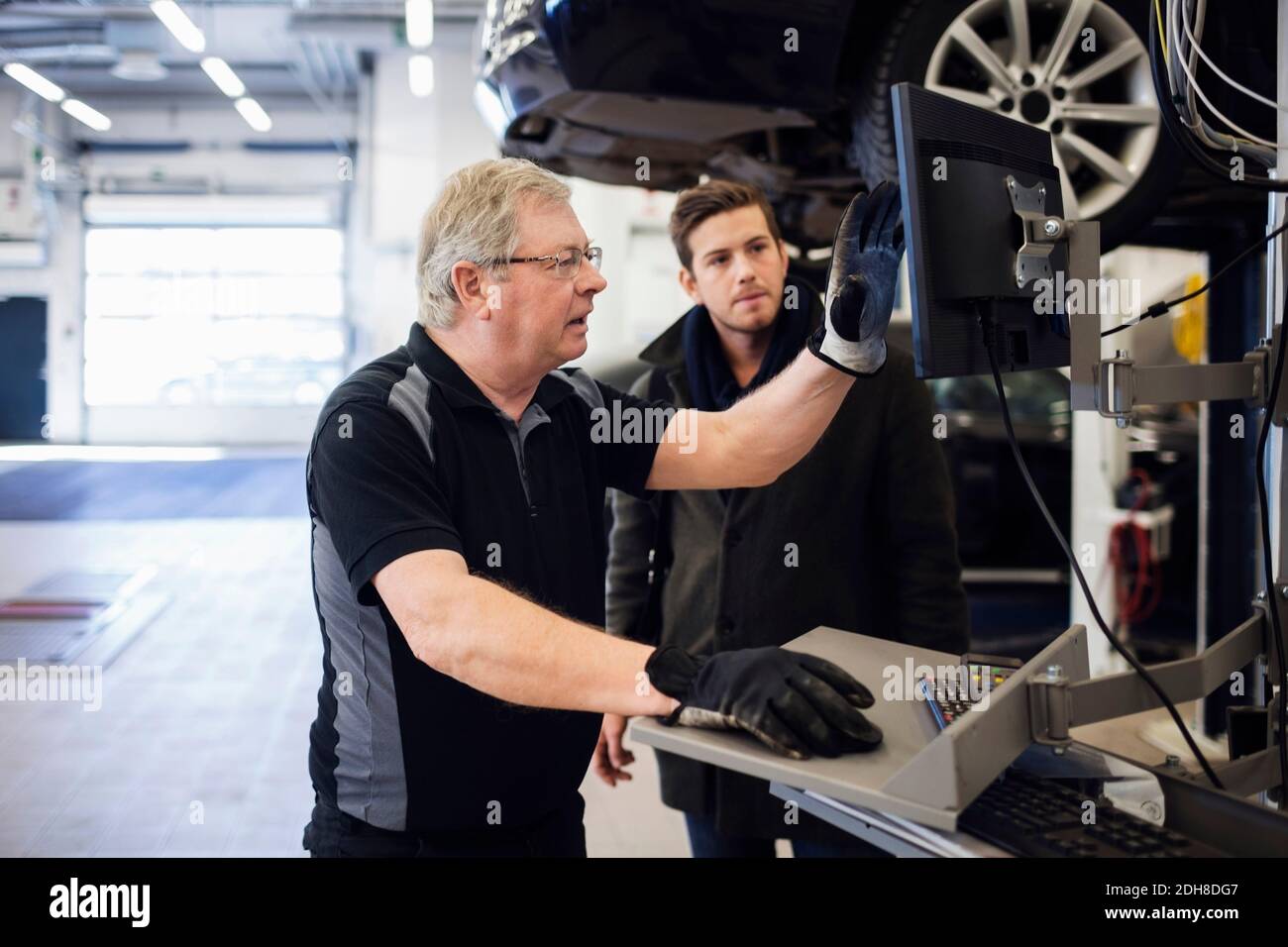 Senior mechanic showing computer monitor while discussing with customer ...
