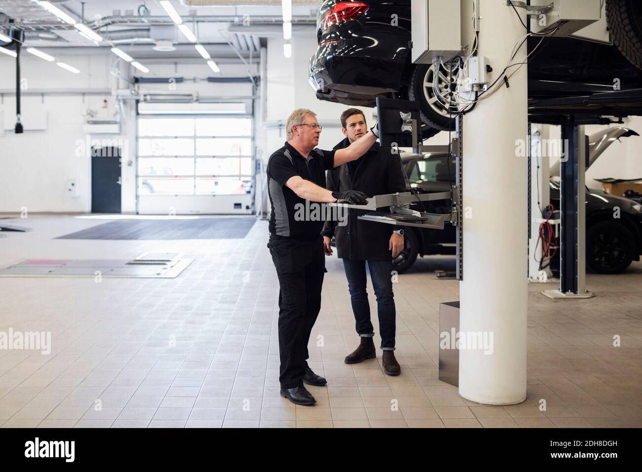 Senior mechanic explaining customer while standing at repair shop Stock ...