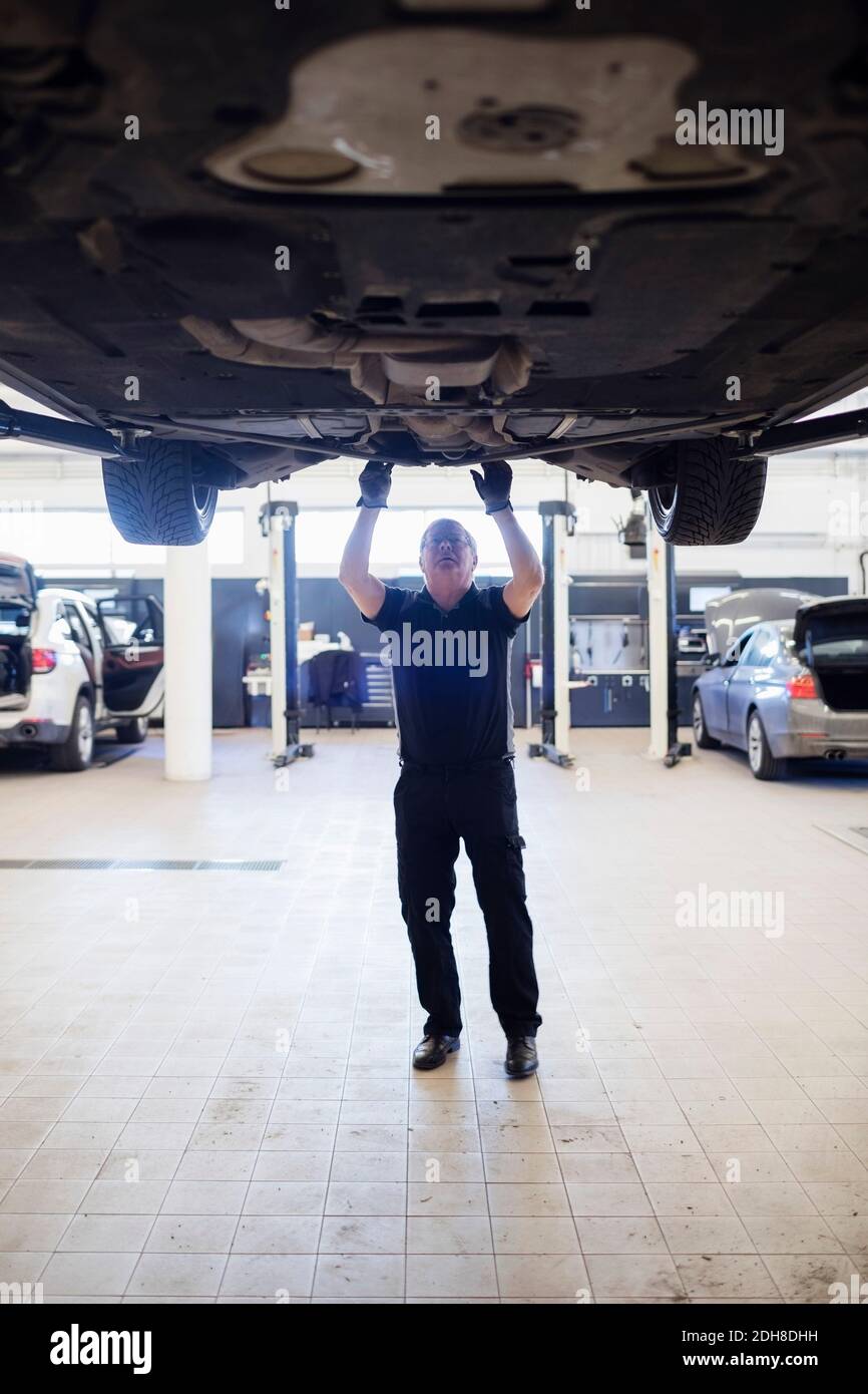 Senior mechanic repairing car while standing under hydraulic platform ...