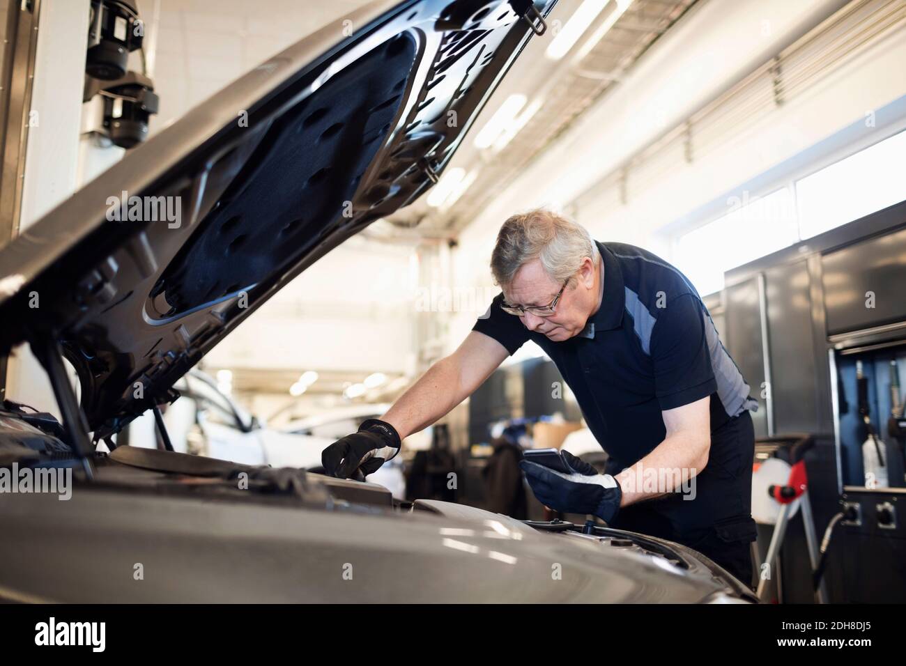 Senior mechanic holding mobile phone while repairing car at shop Stock ...