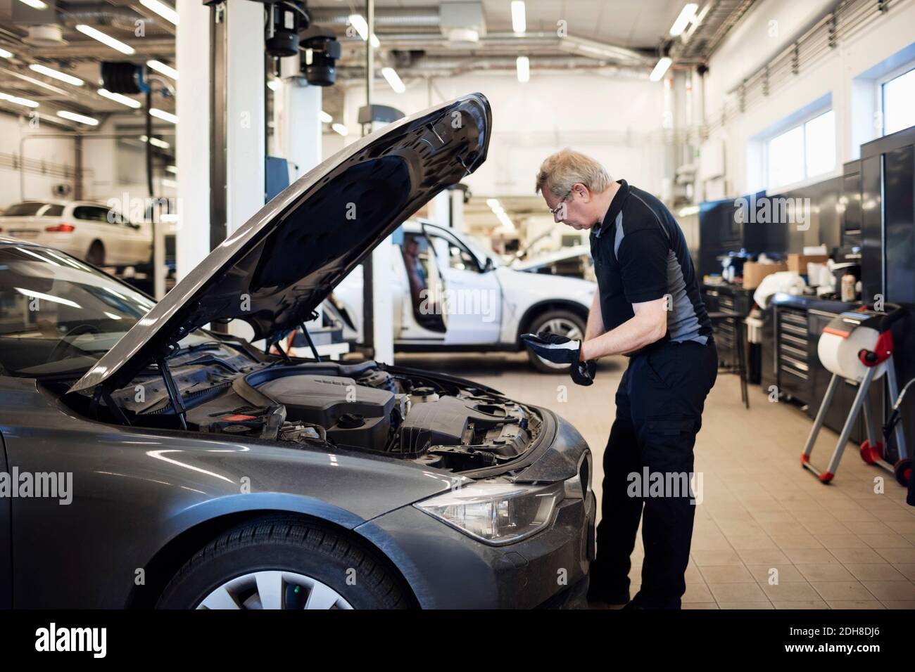 Senior mechanic holding mobile phone examining car at shop Stock Photo ...