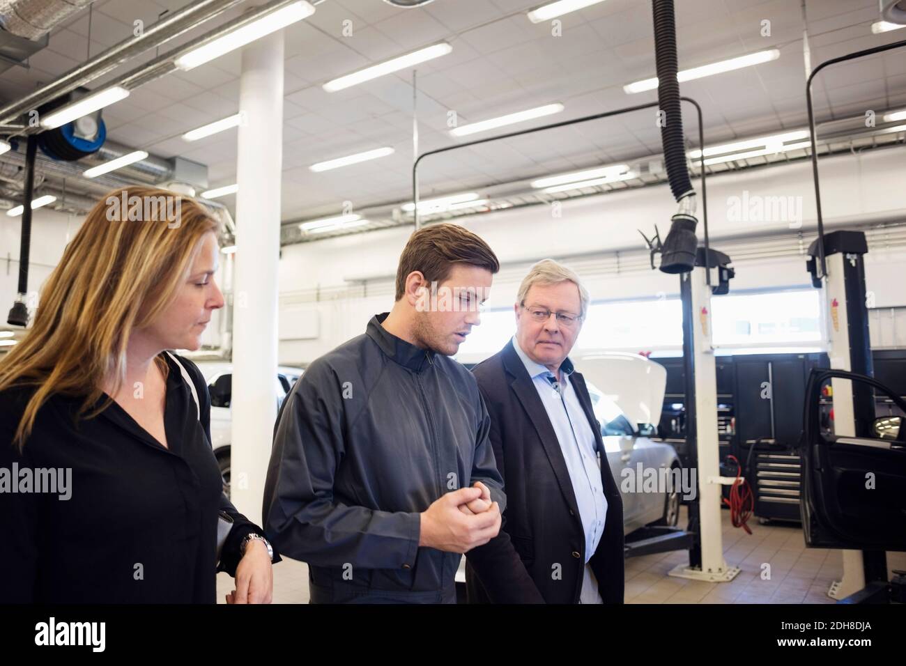 Mechanic discussing with clients while walking in auto repair shop ...