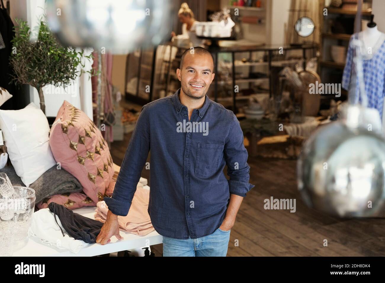 Portriat of smiling male owner standing by clothes on table at store ...