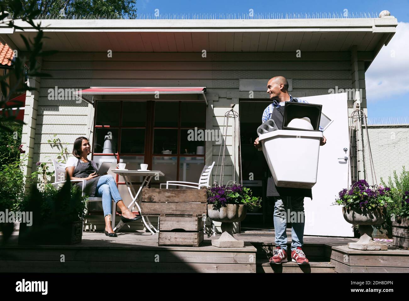 Smiling woman talking to male colleague carrying container outside cafe ...