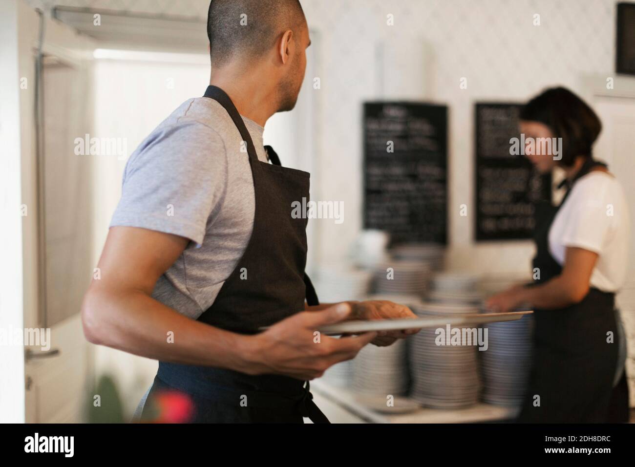 Man holding serving tray looking at female colleague standing by stack ...