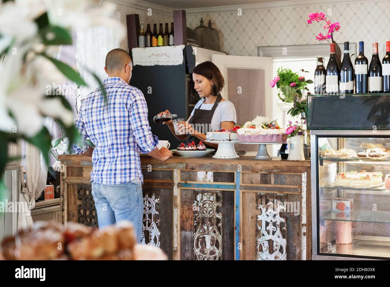 Female owner serving drink in glass for customer at counter in cafe ...