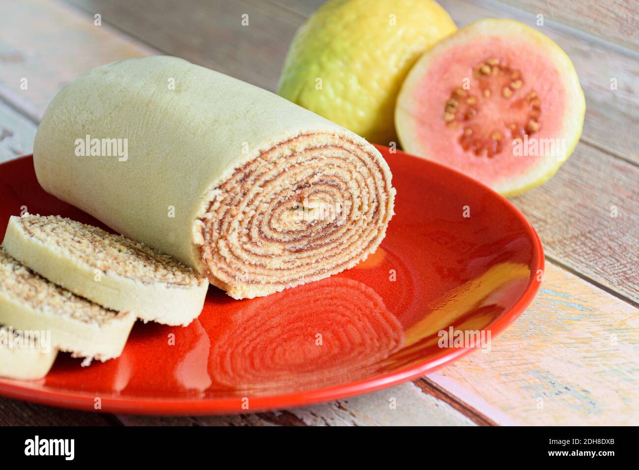 Bolo de rolo (roll cake) sliced on a red plate next to guavas Stock ...