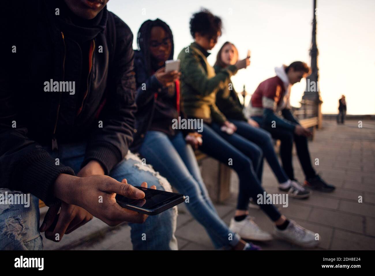 Friends using phone while sitting on railing at city square Stock Photo ...