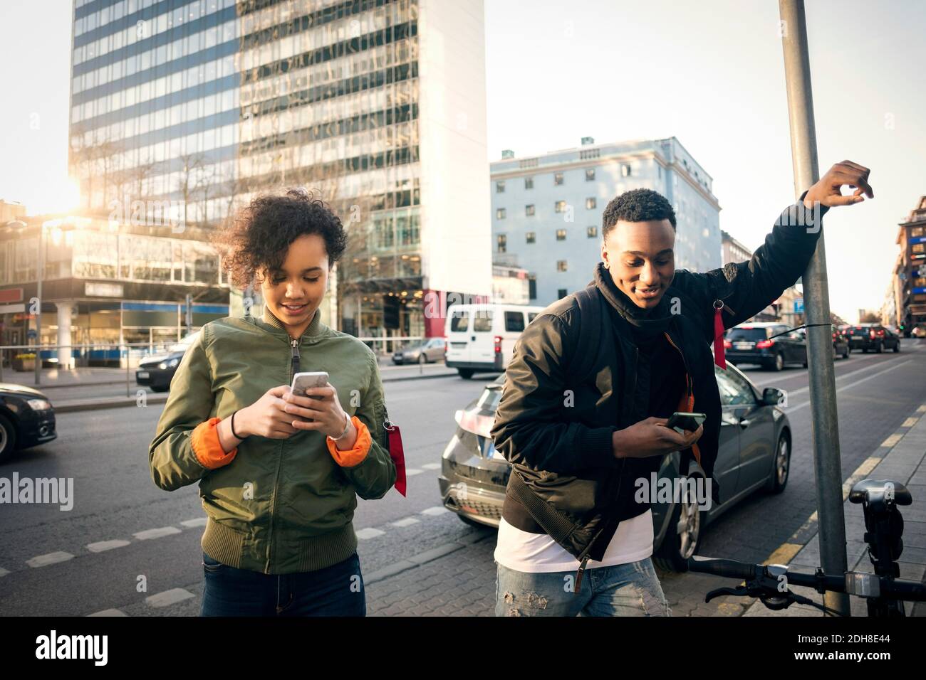 Teenagers using phone while standing on sidewalk by city street Stock ...