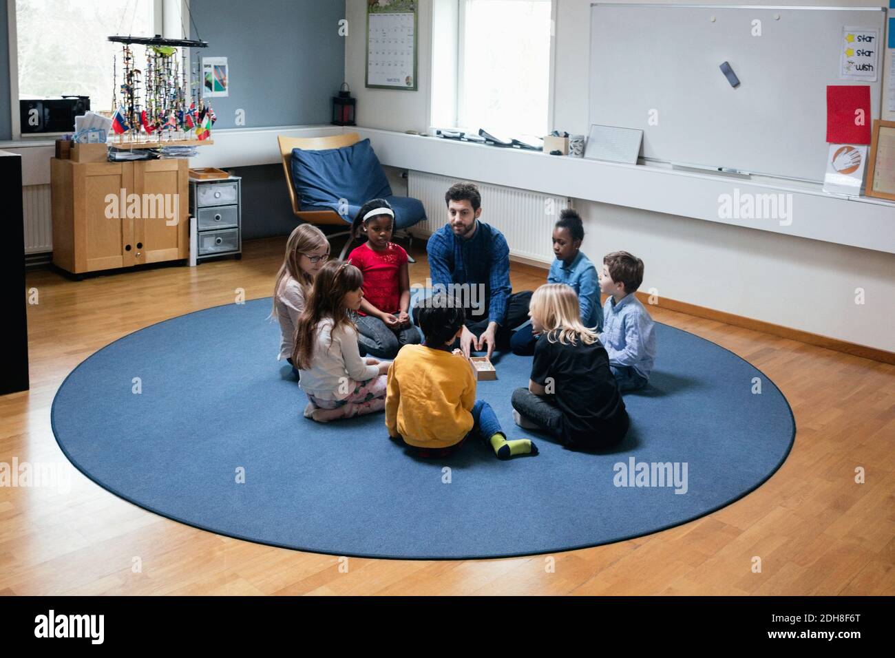 Teacher playing with students while sitting on floor at school Stock ...