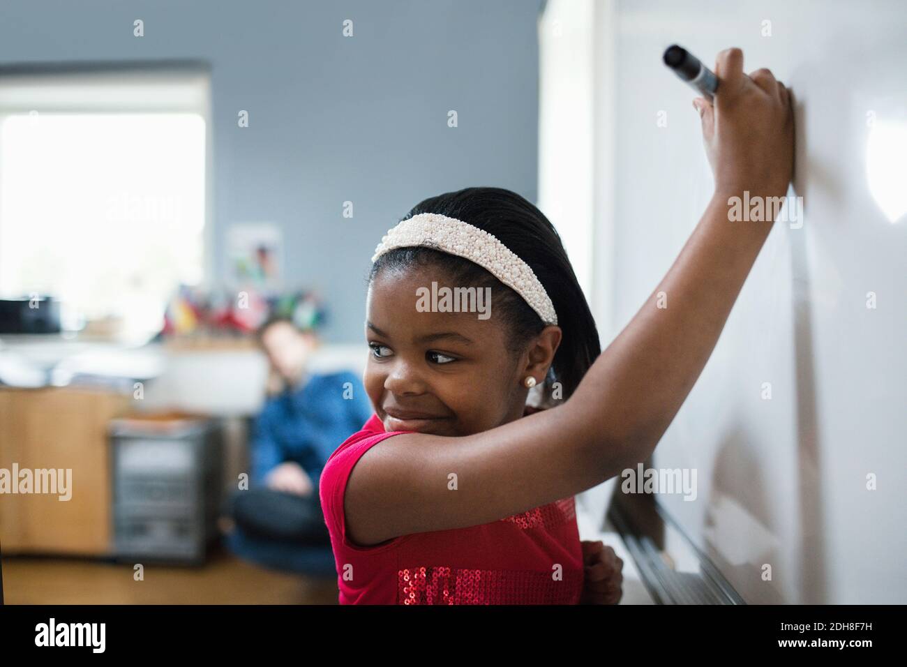 Close-up of girl looking over shoulder while writing on whiteboard in ...