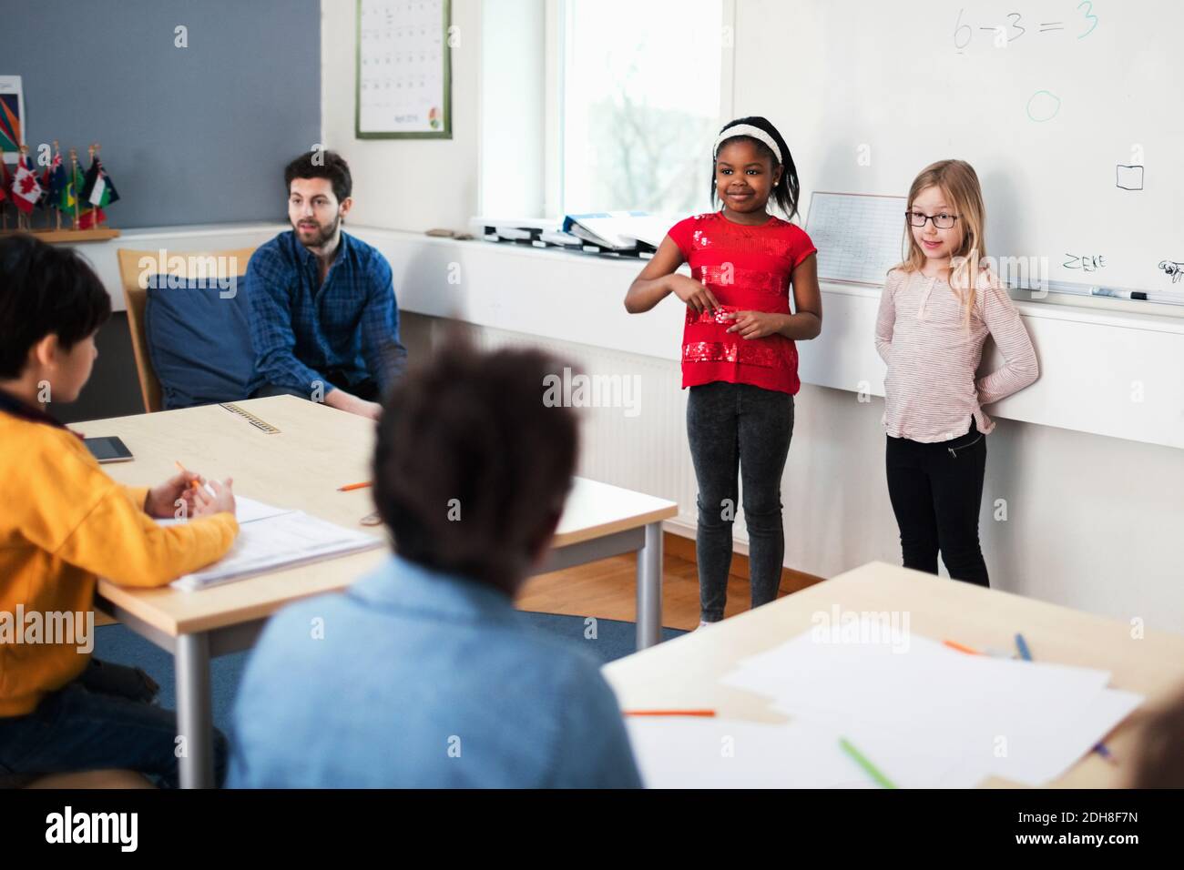Female students standing against whiteboard wile teacher sitting in ...