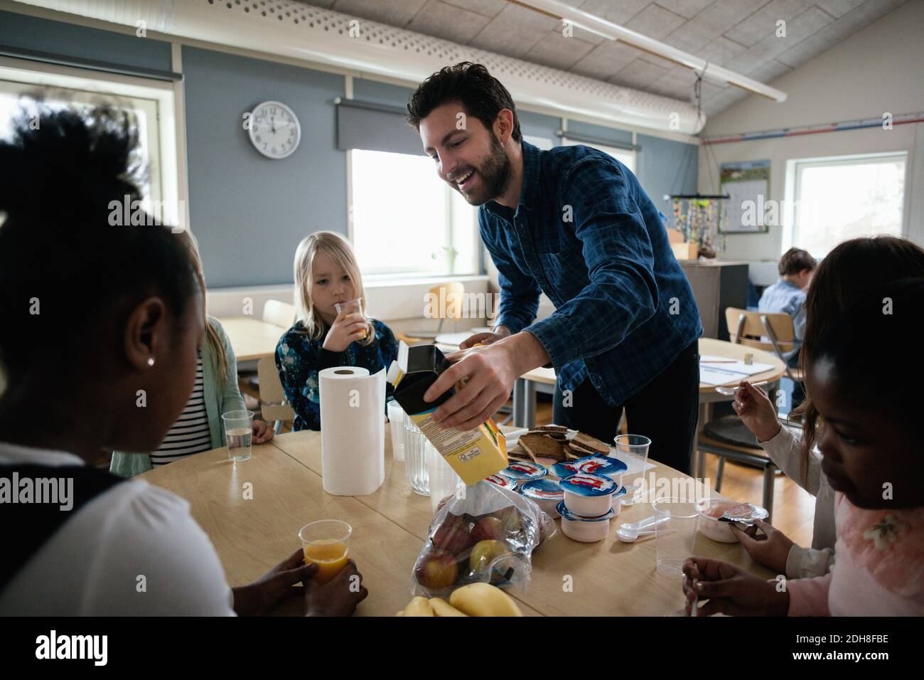 Teacher serving juice to students sitting at table in classroom Stock ...