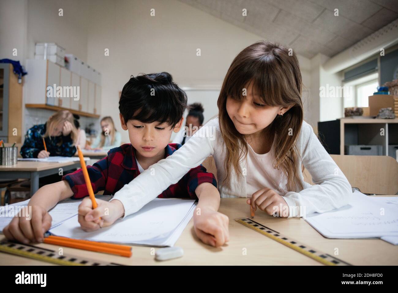 Female friend helping student while studying at desk in classroom Stock ...
