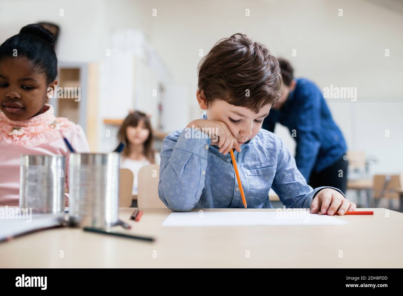 Serious boy studying while teacher standing in background at school ...