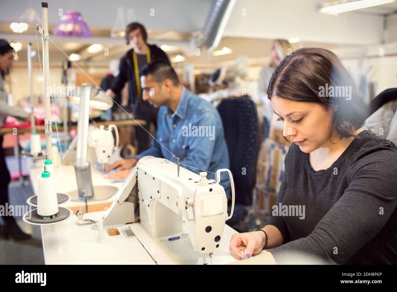 Concentrated woman sewing clothes while volunteers working at workshop ...