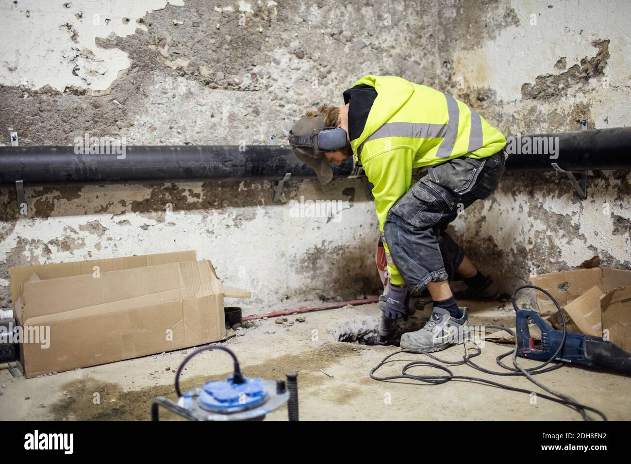 Concentrated plumber drilling floor by pipes in basement Stock Photo ...